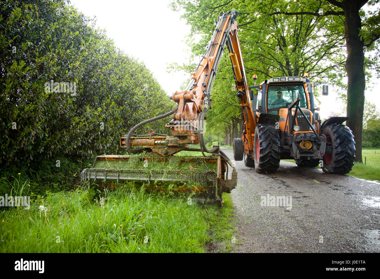 mowing grass shoulder along road in public space with big orange ...