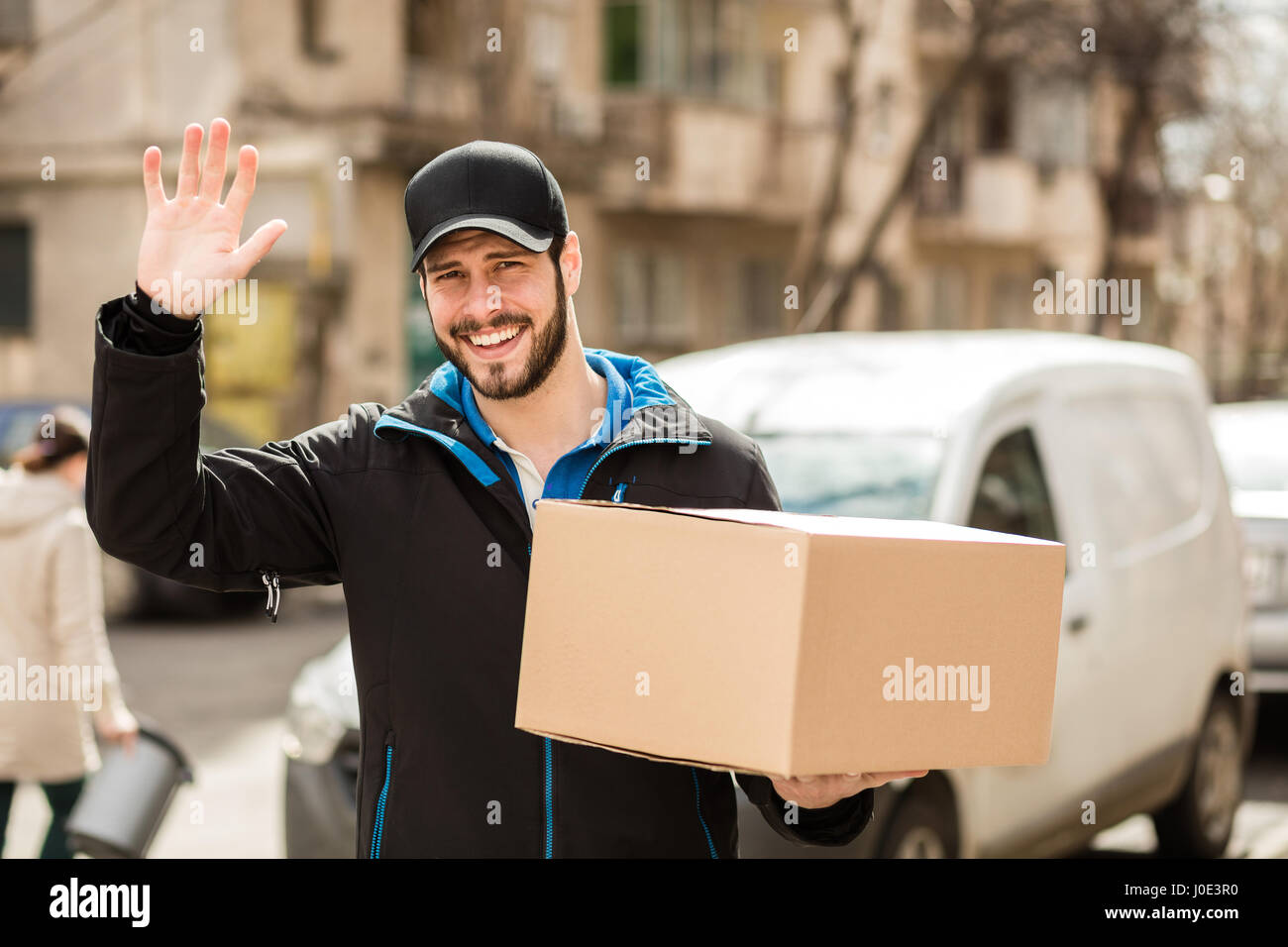 Delivery man with cap and cardboard in hands saying hello to camera ...