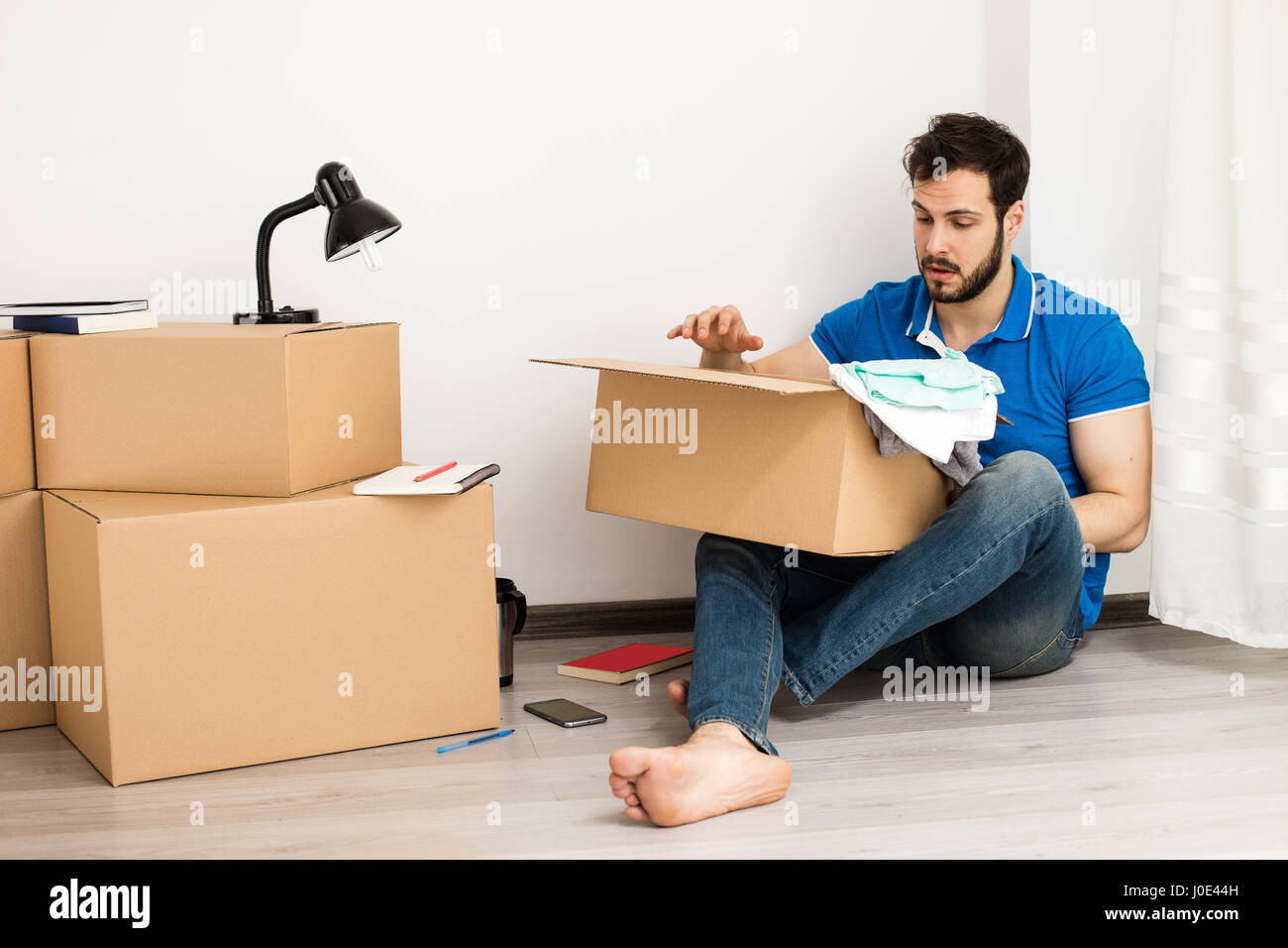 young man lying on the floor and packing his stuff in order to move ...