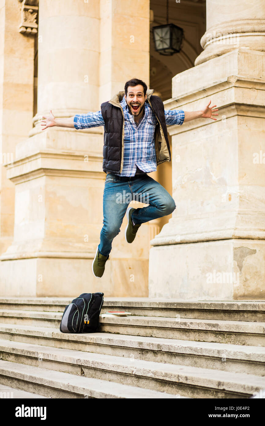 happy young man jumping up for joy on the stairs of a building with ...