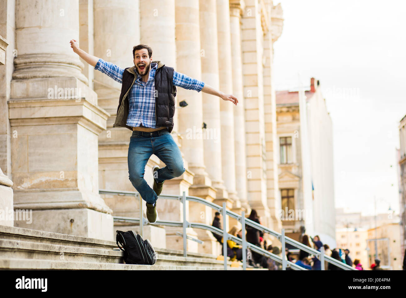 happy young man jumping up for joy on the stairs of a building with ...