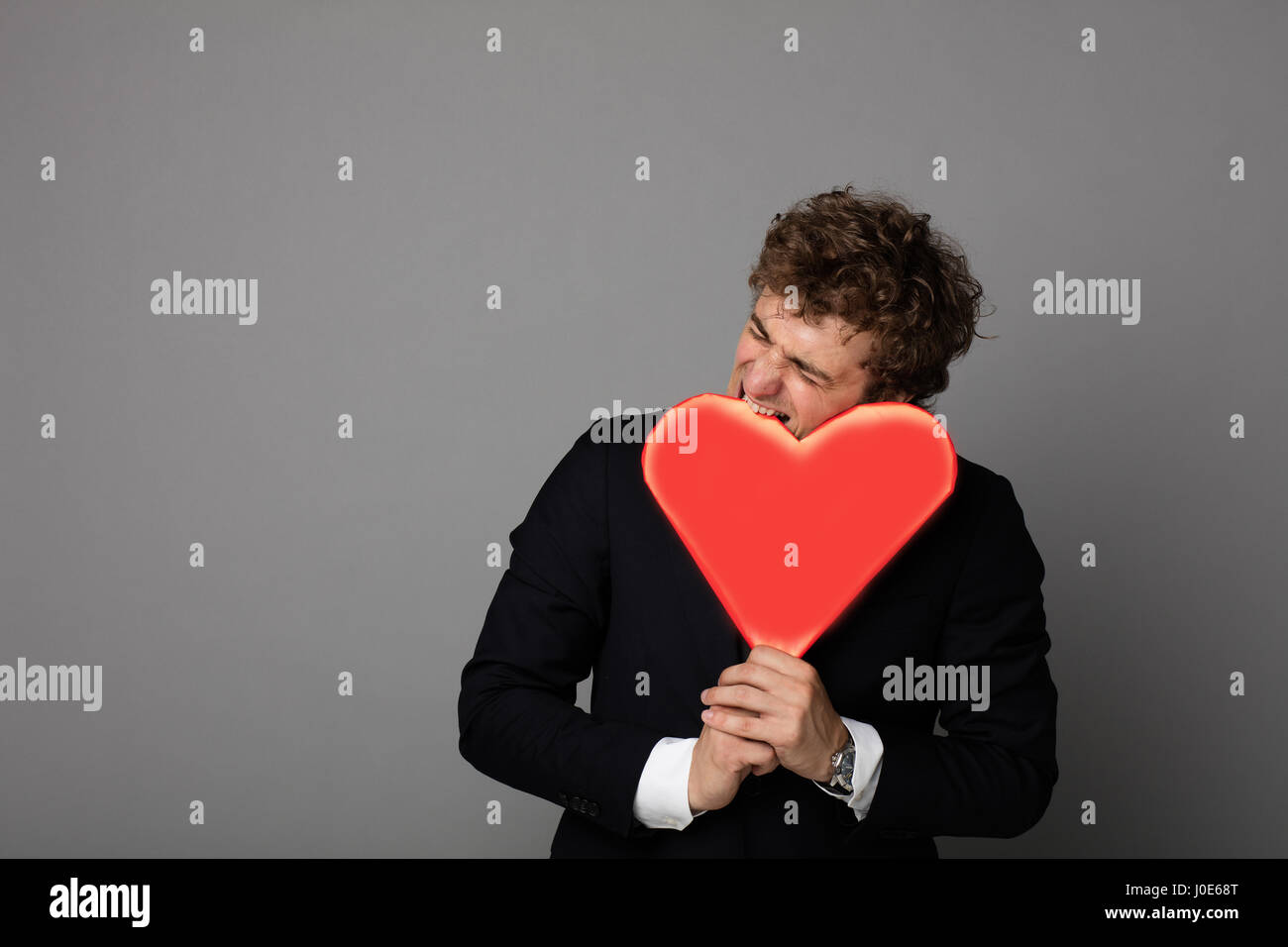 broken heart concept with a curly handsome men biting his red heart on ...