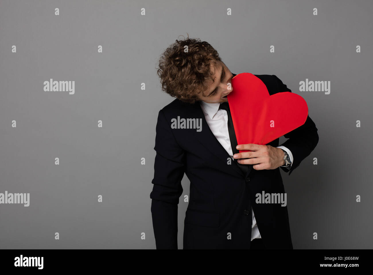 broken heart concept with a curly handsome men biting his red heart on ...