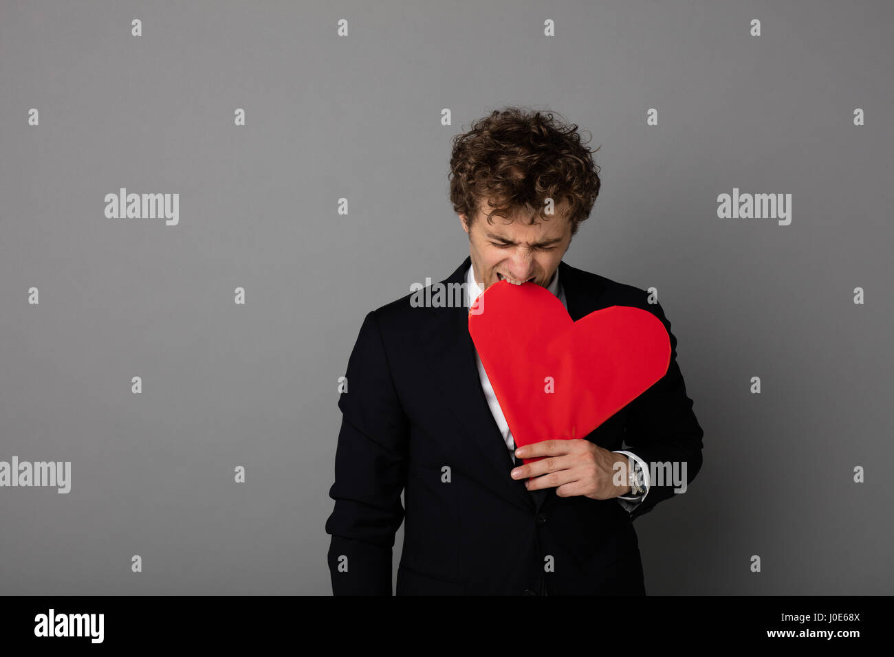 broken heart concept with a curly handsome men biting his red heart on ...