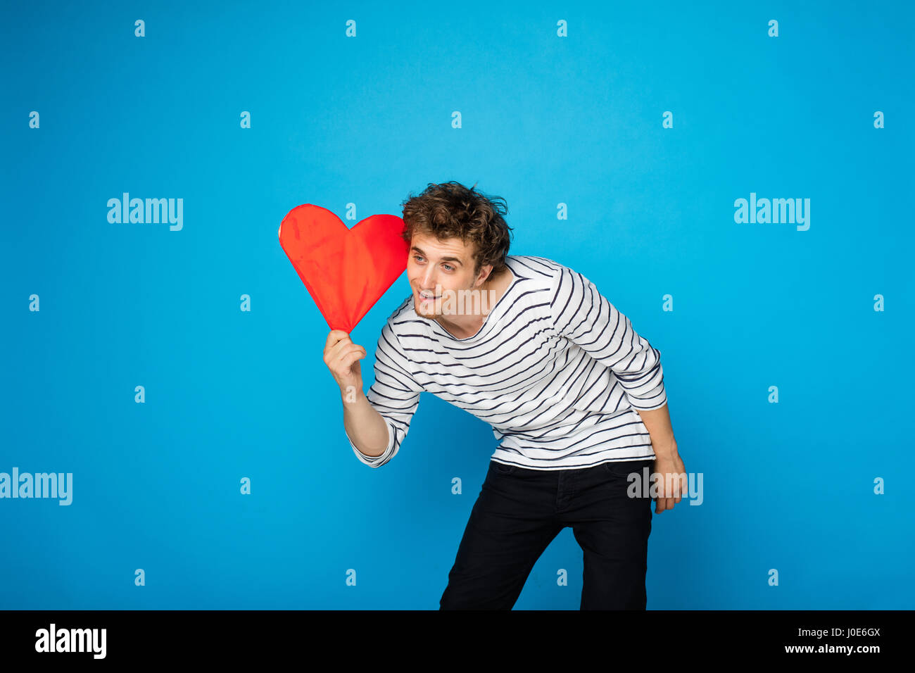 young curly lively guy with sailor shirt listening a red heart on blue ...