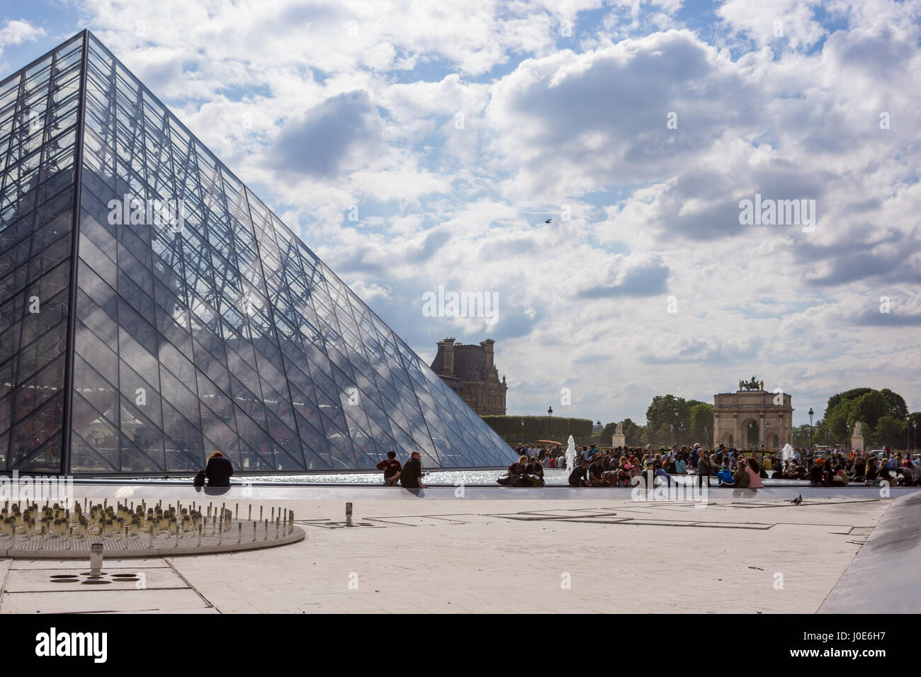Crowds of people sitting around the fountain near The Louvre pyramid on ...