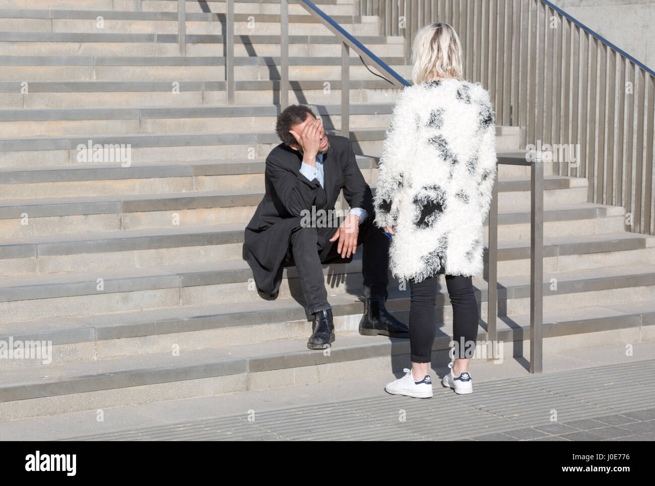 White adult woman standing next to sitting in stairs man and arguing ...