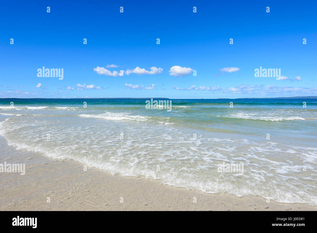 Gentle rolling waves and fluffy clouds at Callala Beach, a sandy and ...