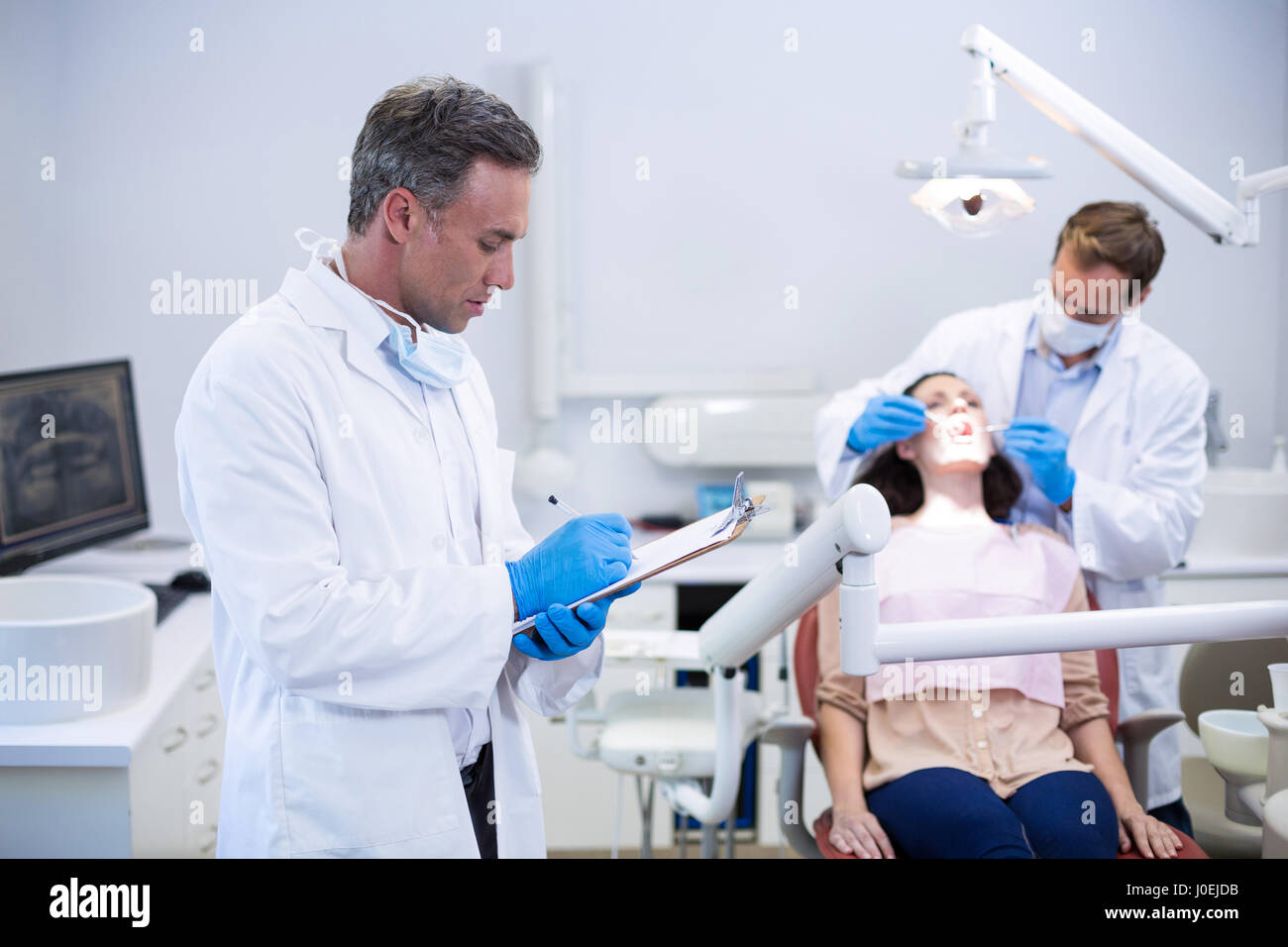Dentist writing on clipboard in dental clinic Stock Photo - Alamy