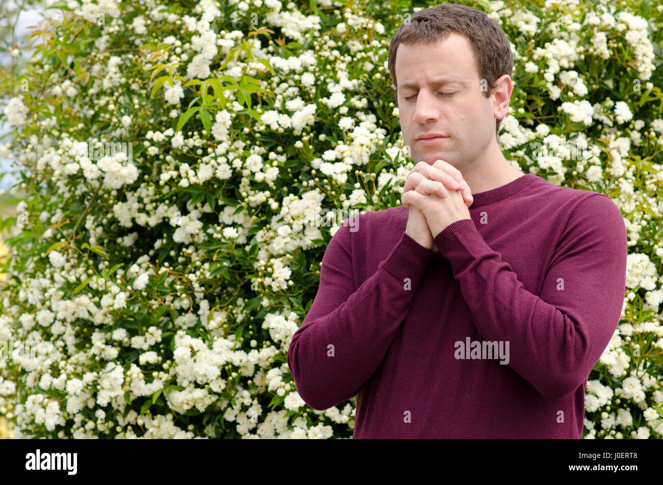 Man praying outdoors with his hands together in front of a flowering ...