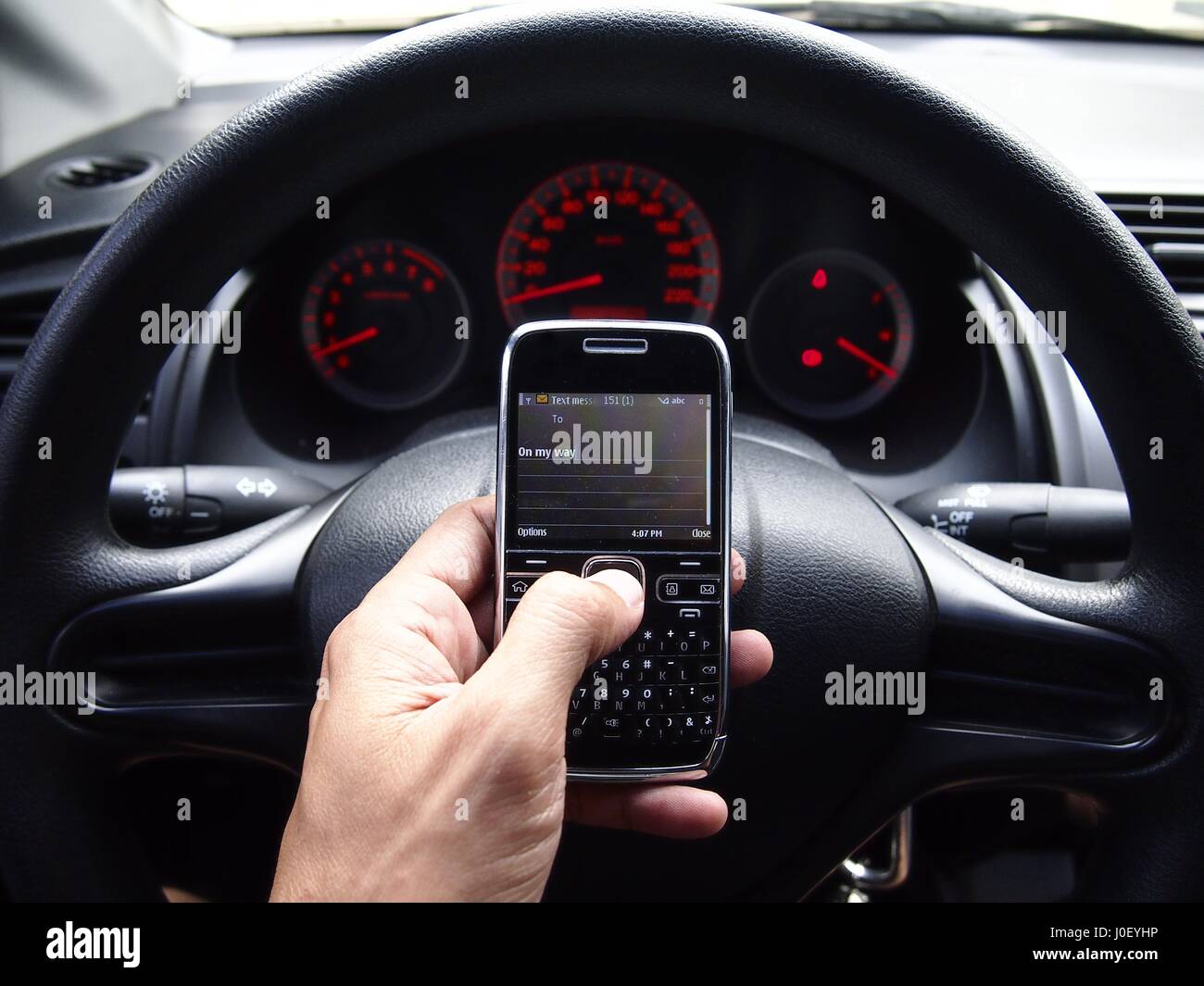 Photo of a hand holding a cellphone in front of a steering wheel of a ...
