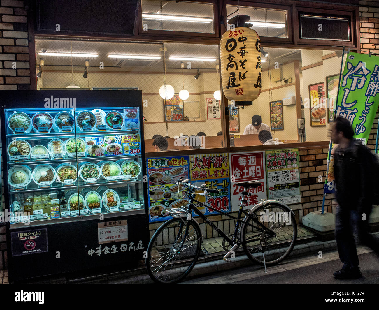 Man walking by restaurant diner, with bicycle and showcase of shokuhin ...
