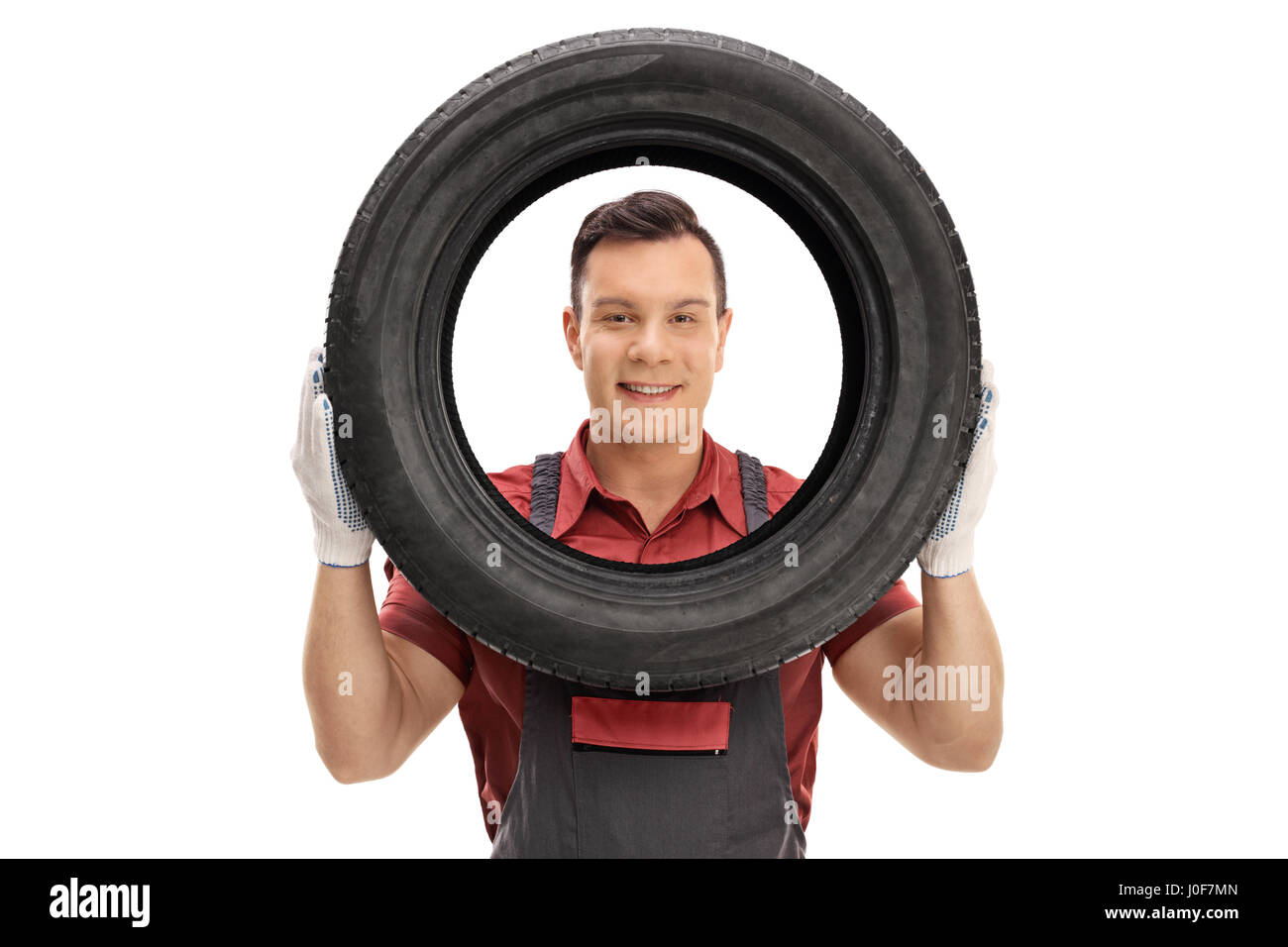 Mechanic looking at the camera through a tire isolated on white ...
