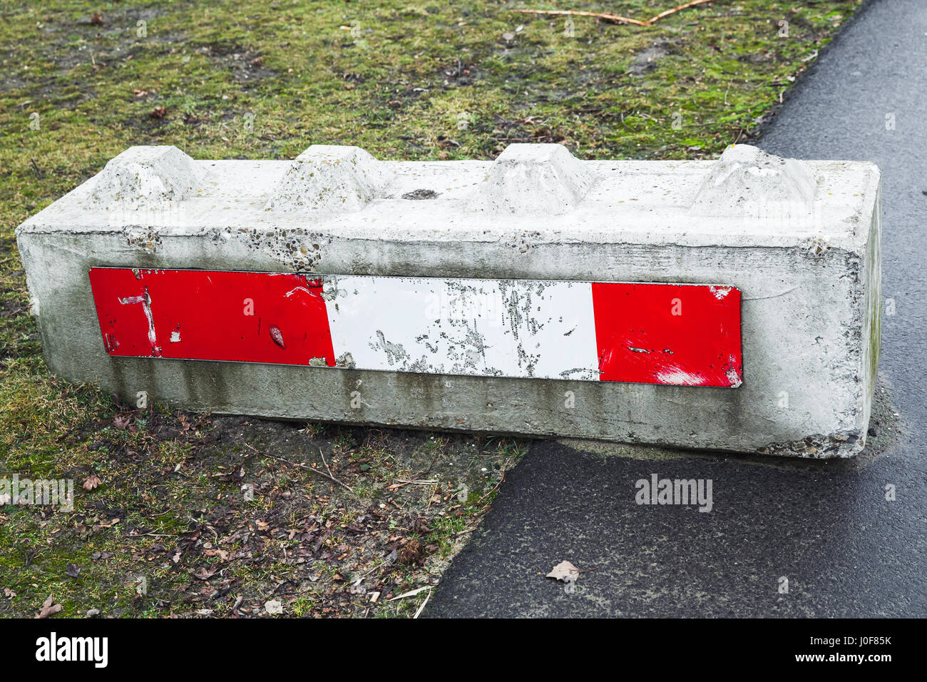 Concrete road block with red white striped warning sign lays on the ...