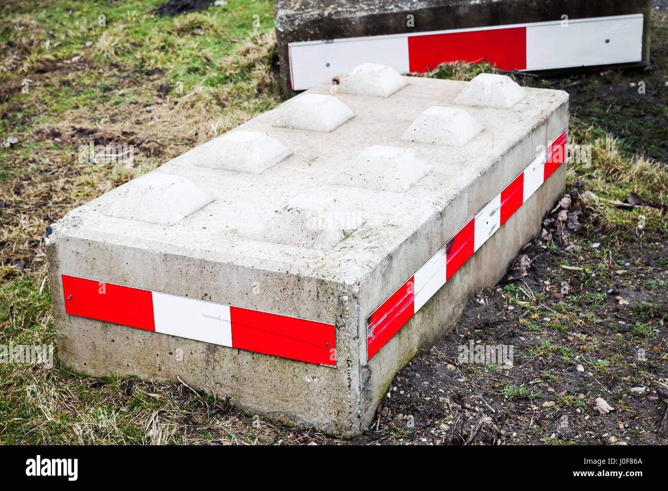 Concrete road blocks with red white striped warning signs lay on green ...