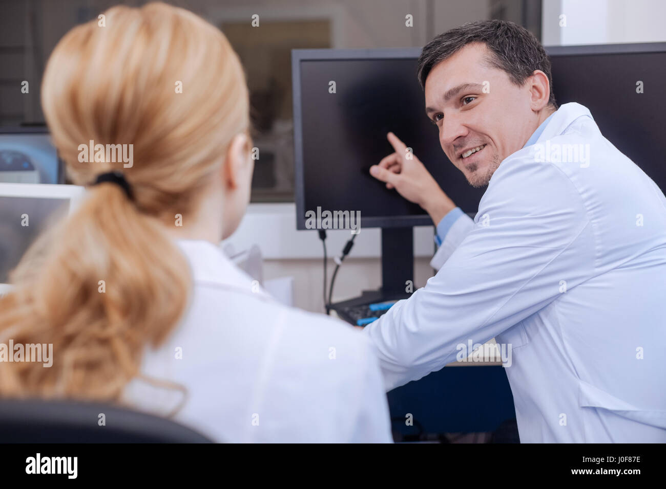 Pleasant happy doctor pointing at the monitor Stock Photo - Alamy