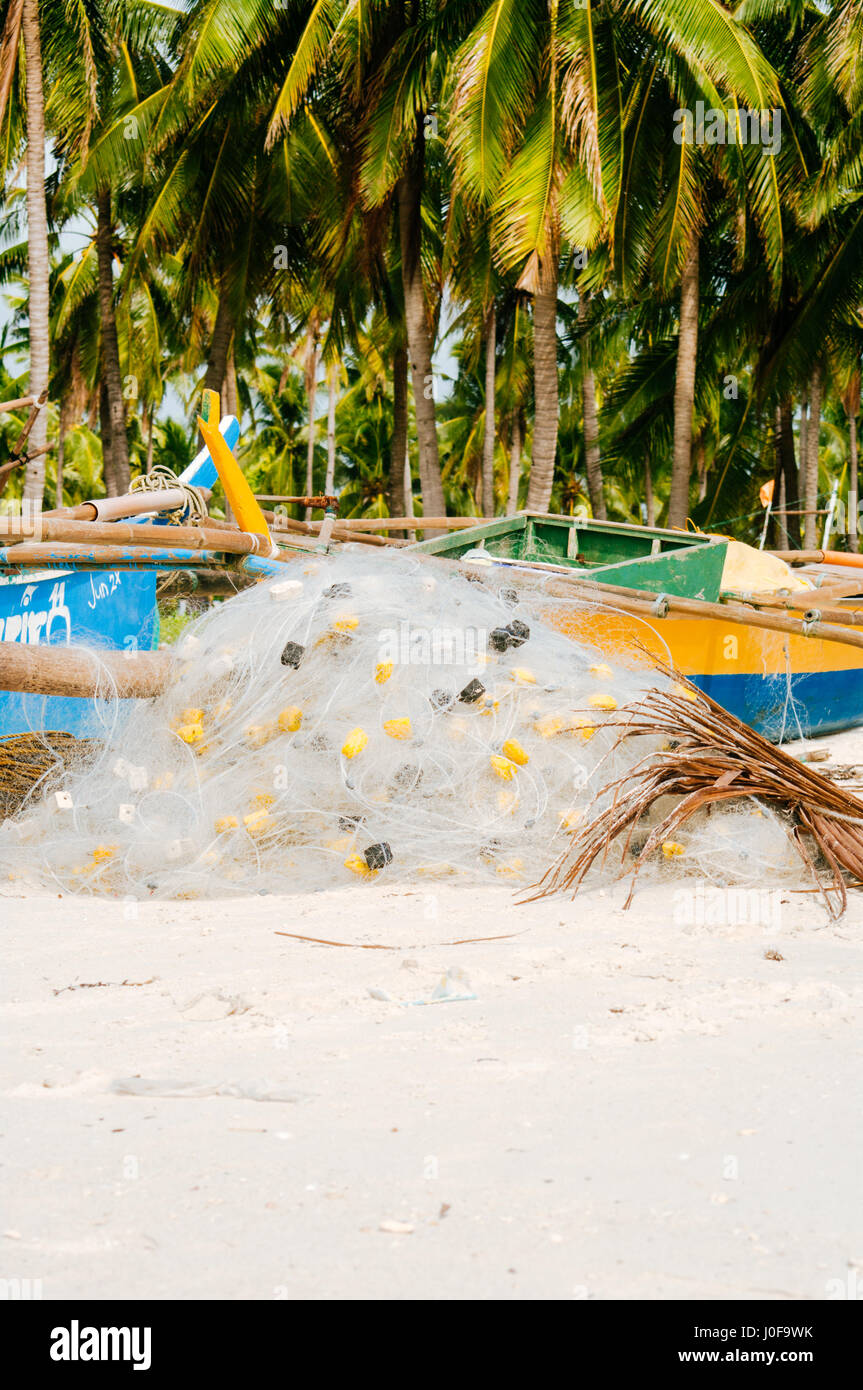 White fishing net on coral sand beach with colorful boats and palms in ...