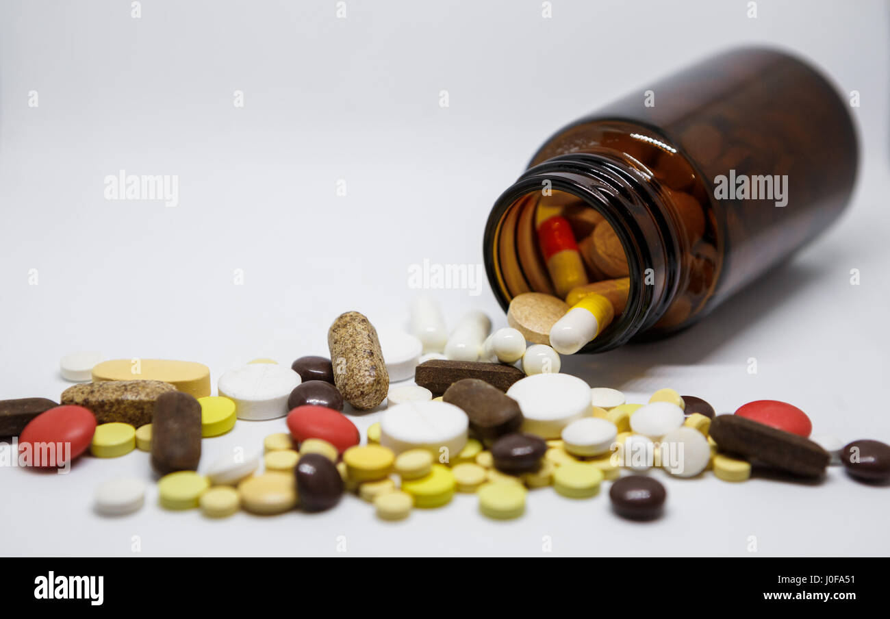 Pile of multicolored tablets and medicine lying on a white surface ...