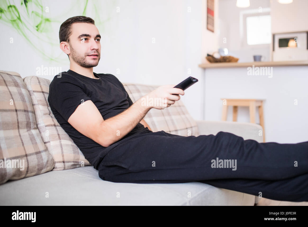 Man with remote control on sofa at home Stock Photo - Alamy
