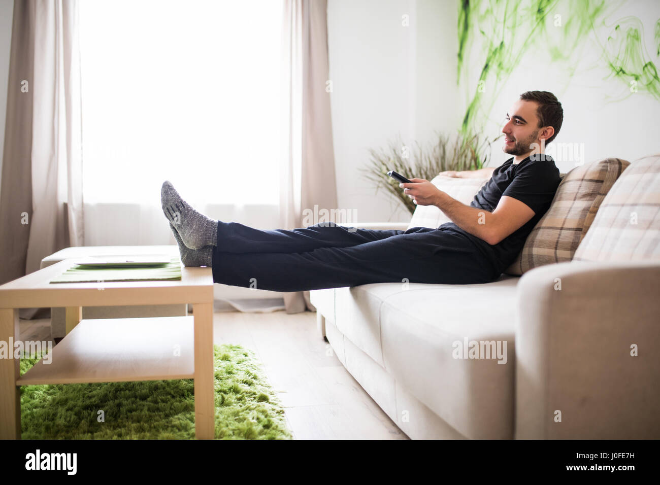 Rear view of young man using remote control while sitting on couch in ...