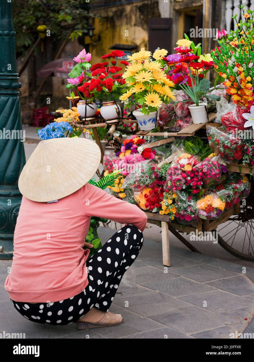 Vertical portrait of a lady selling flowers from the back of a bicycle ...