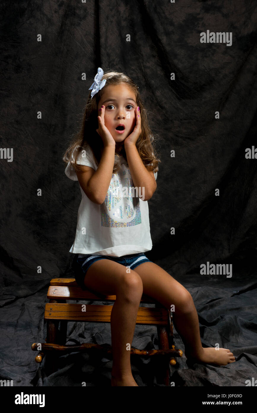 little girl modeling in studio brown background siting on a wood chair ...