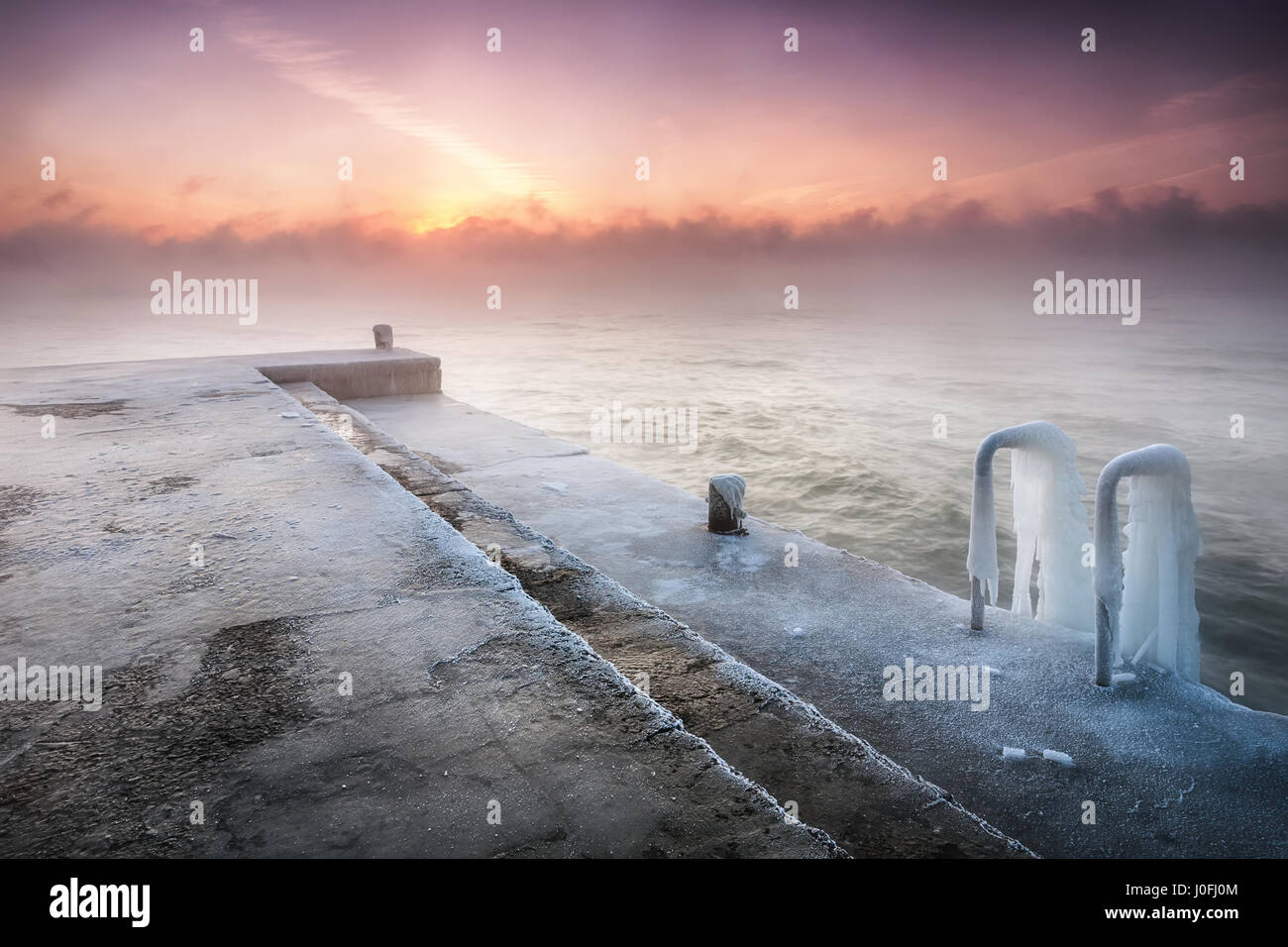 Frozen bridge platform with icy ladder in the cold sea at sunrise Stock ...