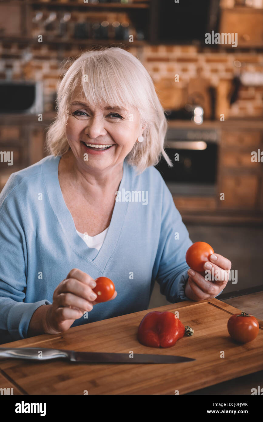 Happy senior woman holding tomatoes while cooking at kitchen Stock ...