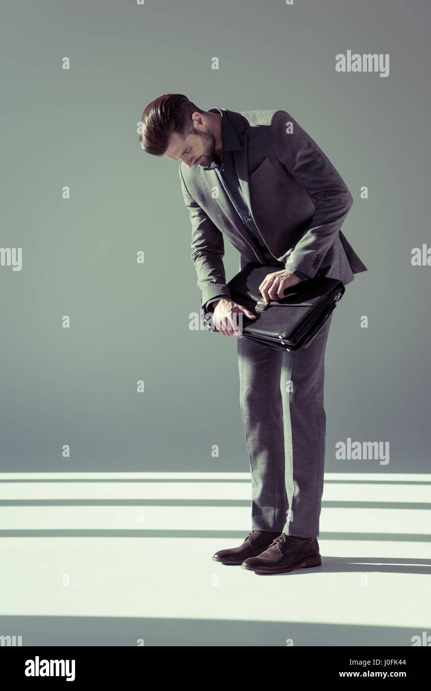Handsome businessman in stylish suit opening briefcase on grey Stock ...