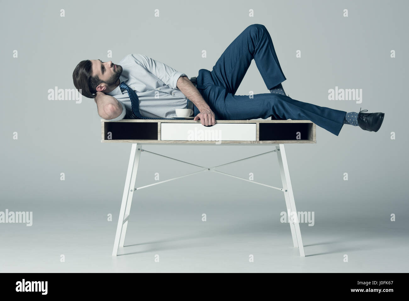 side view of businessman lying on table with cup of coffee on grey ...