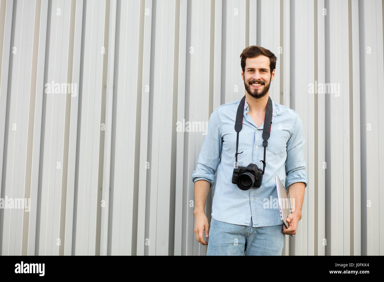 handsome photographer standing outside on gray background with laptop ...