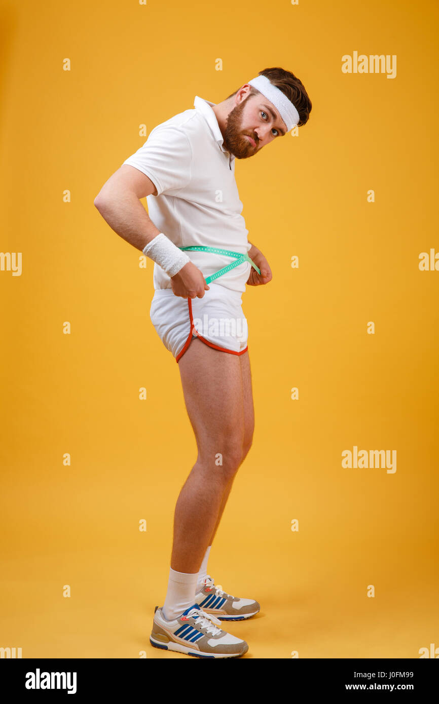 Full length portrait of a sad unsatisfied fitness man measuring his ...