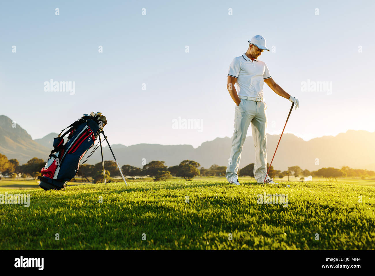 Full length of young man standing on golf course at sunset ...