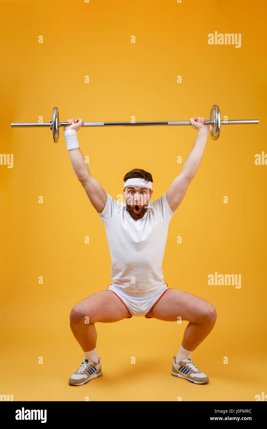 Full length portrait of a fitness man squatting with barbell isolated ...