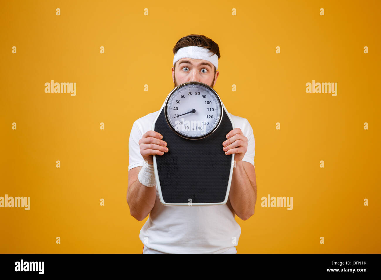 Portrait of a scared fitness man hiding behind weight scales and ...