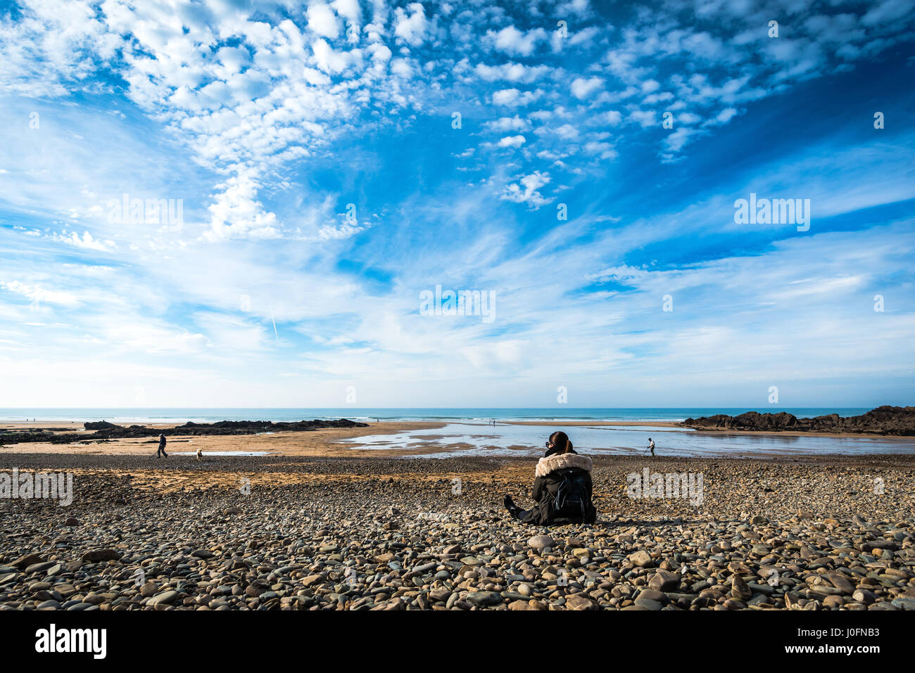 Woman sitting alone watching the ocean on a beach in Bude, Cornwall, UK ...