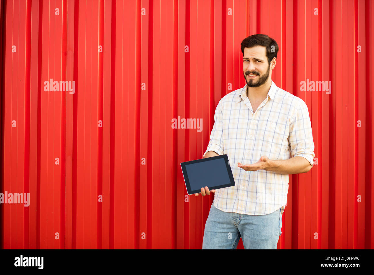 handsome adult man presenting the screen of his tablet on a red ...