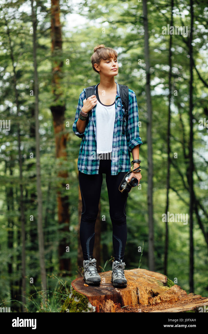 single traveler woman sitting on a log with her backpack and camera in ...