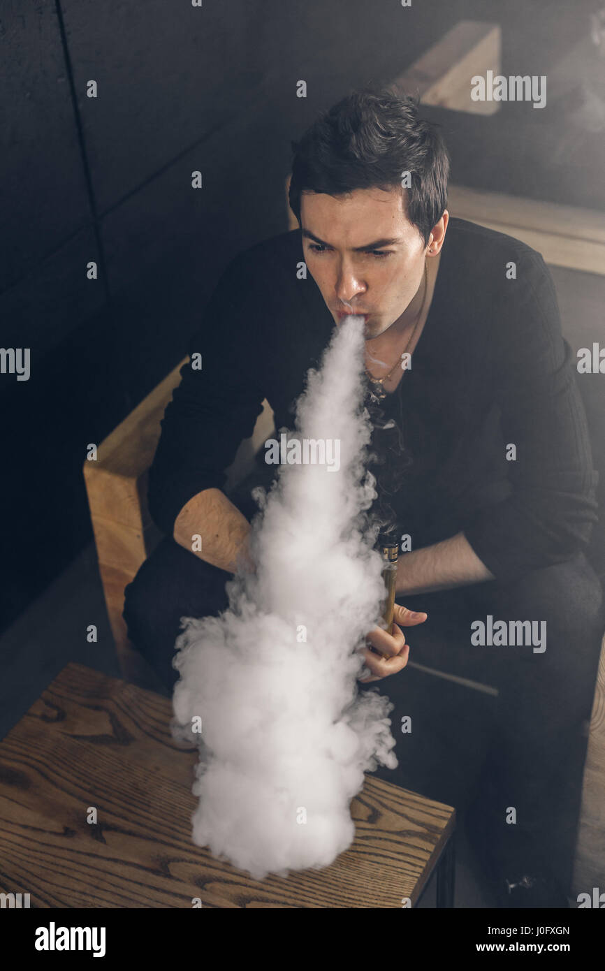 Vaping man holding a mod. A cloud of vapor. Black background Stock ...