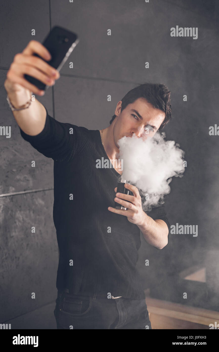 Vaping man holding a mod. A cloud of vapor. Black background Stock ...