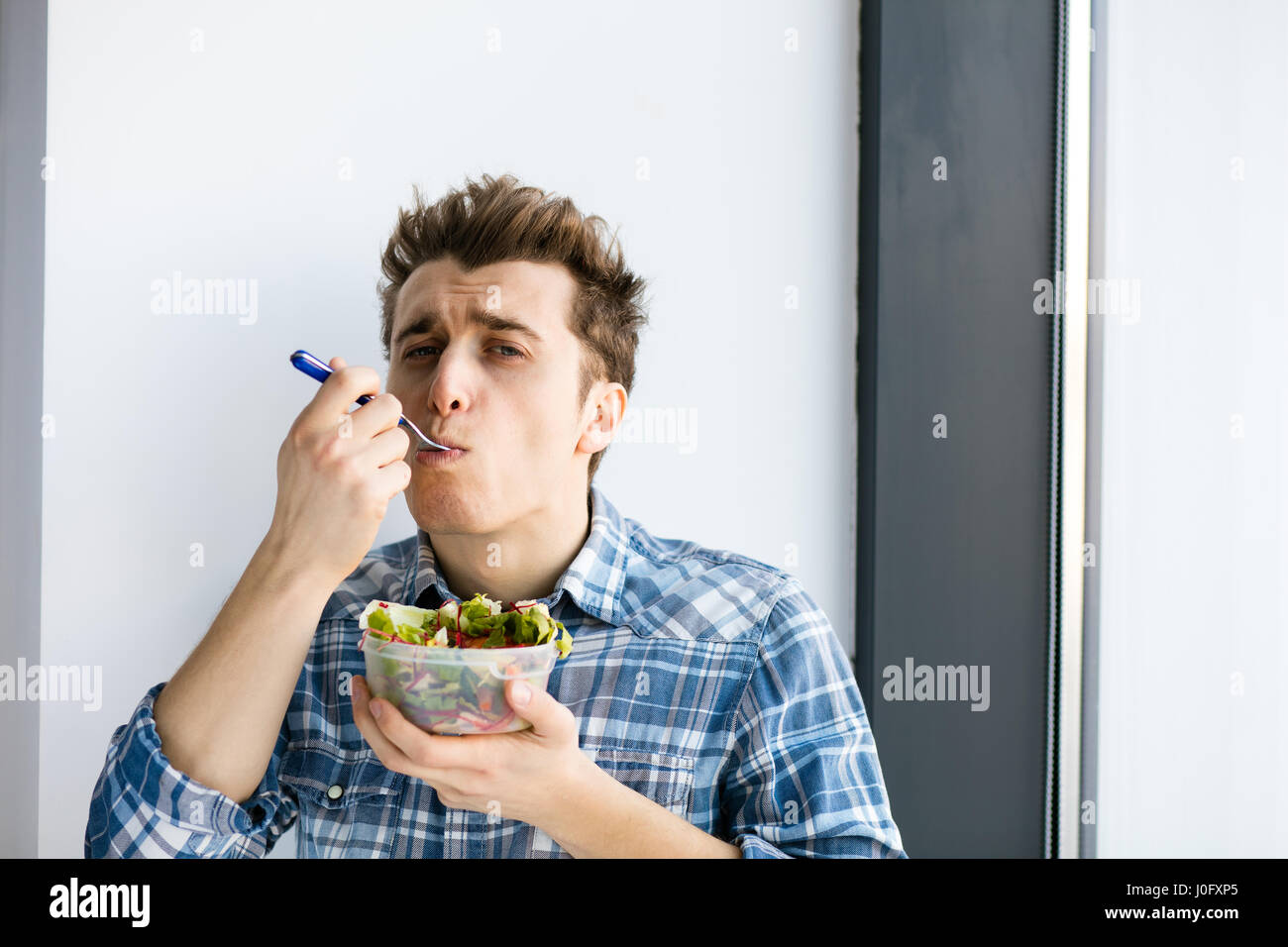 young man eating his vegan salad from a plastic box, his take away ...