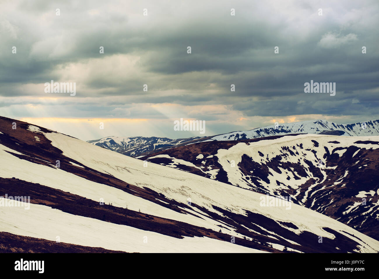 Spring mountain landscape with snow and grass. Dramatic clouds lying on ...