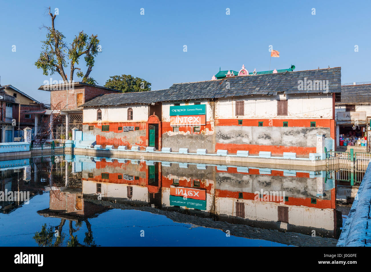 Old buildings reflected in the village tank (pond) in Pragpur, a ...