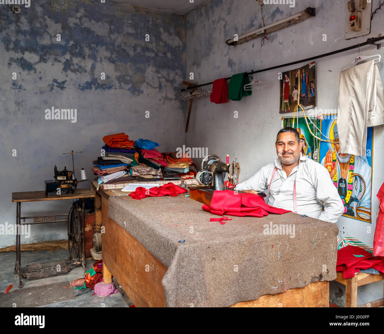 Friendly local Indian tailor working at a traditional sewing machine ...