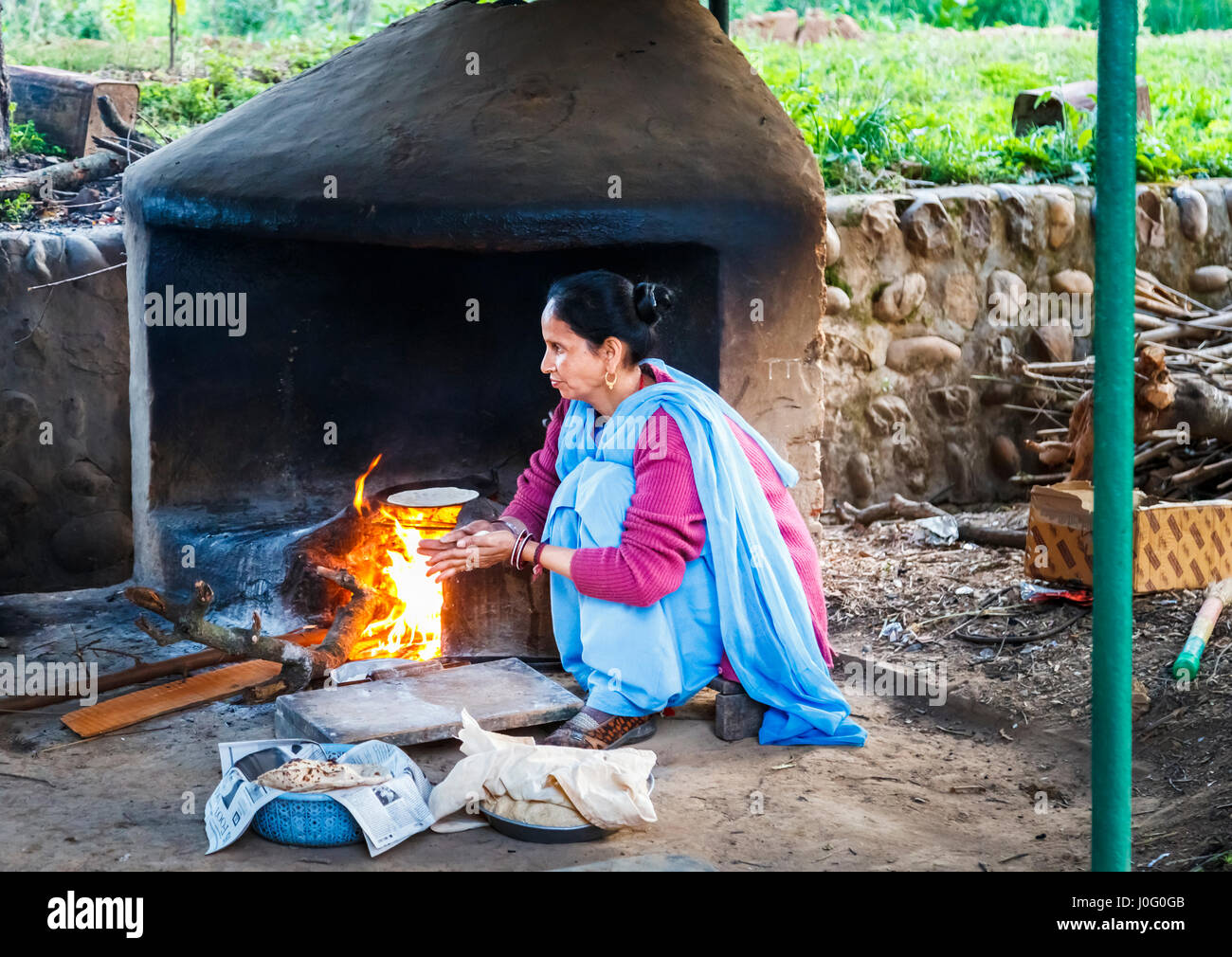 Local Indian woman wearing blue sari cooking chapatis in an oven with ...