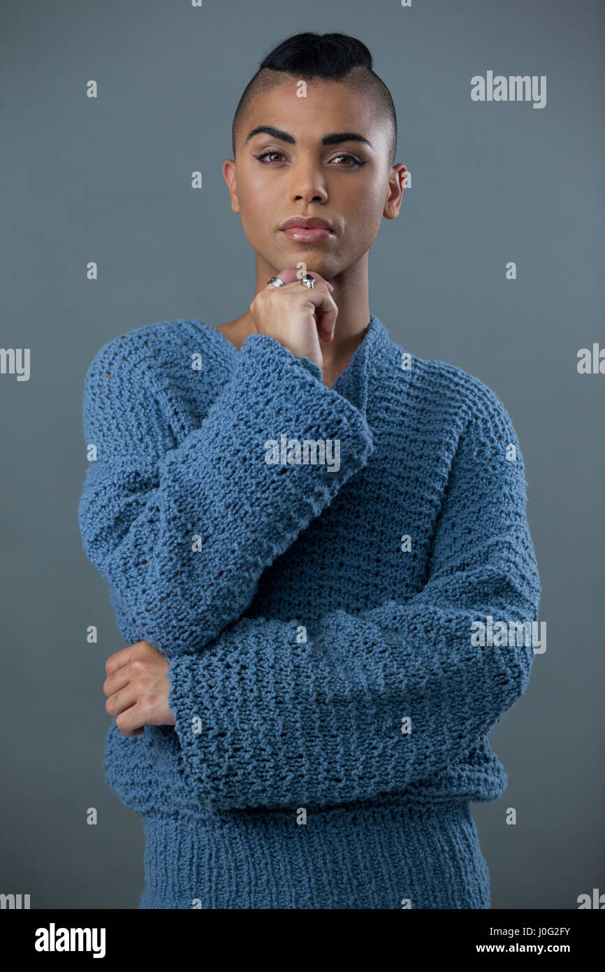 Portrait of transgender woman with hand on chin against gray background ...