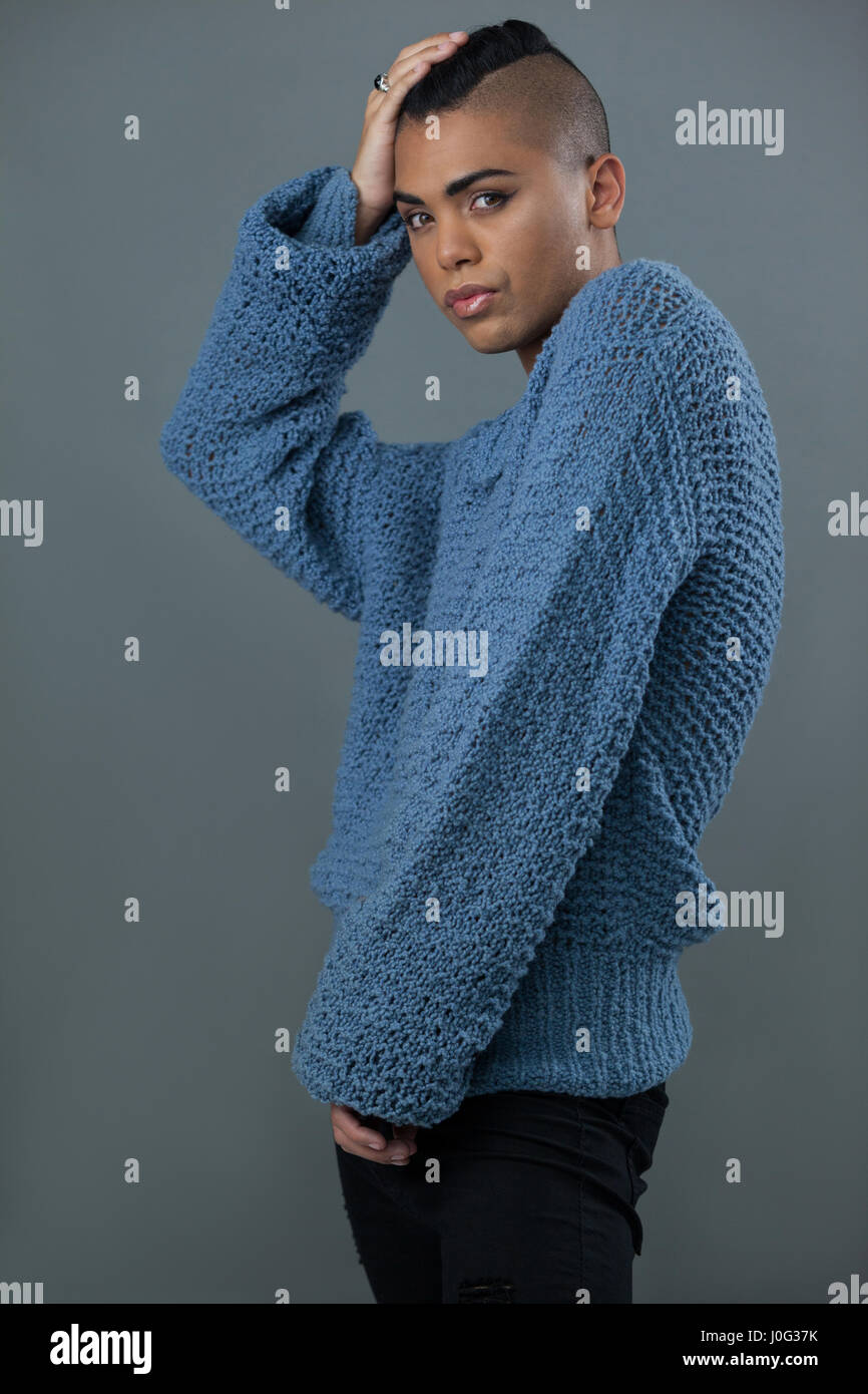 Portrait of transgender woman with hand in hair against gray background ...