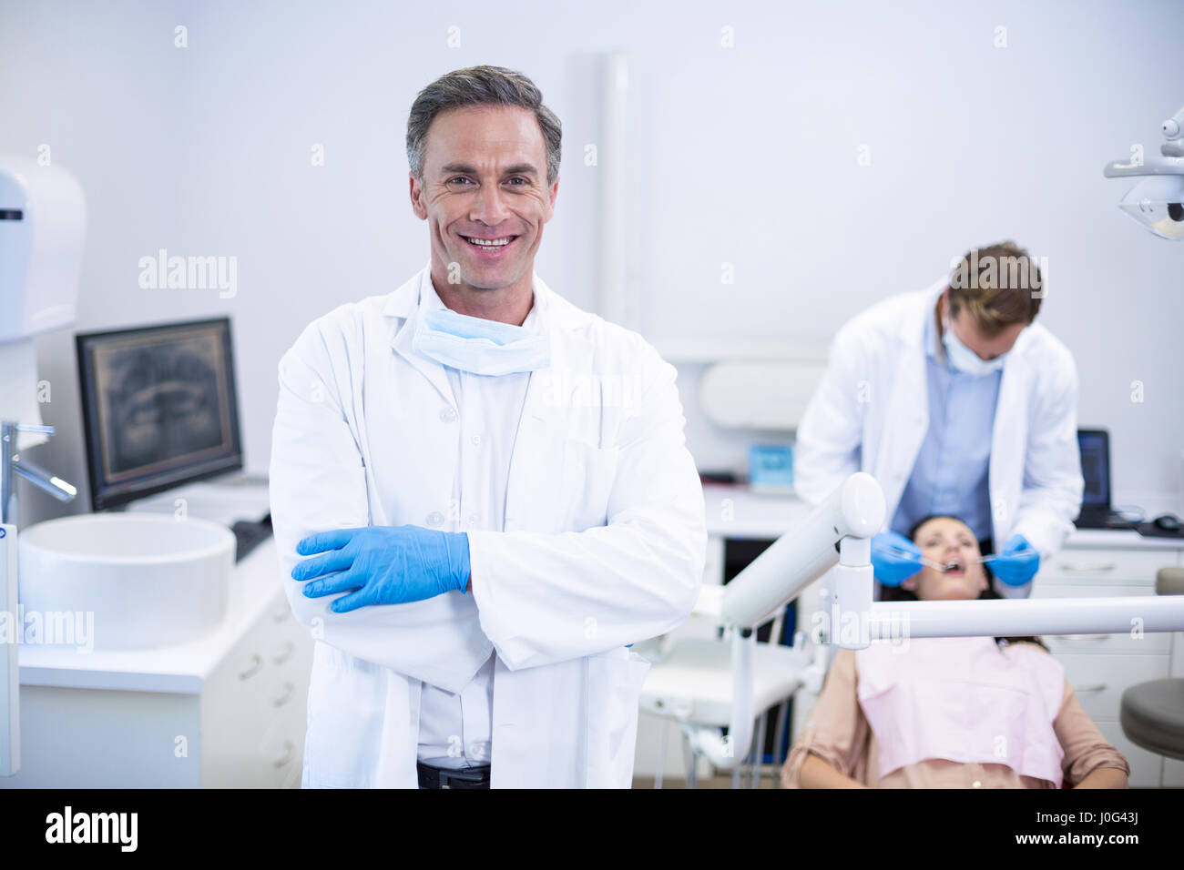 Portrait of smiling dentist standing with arms crossed in dental clinic ...