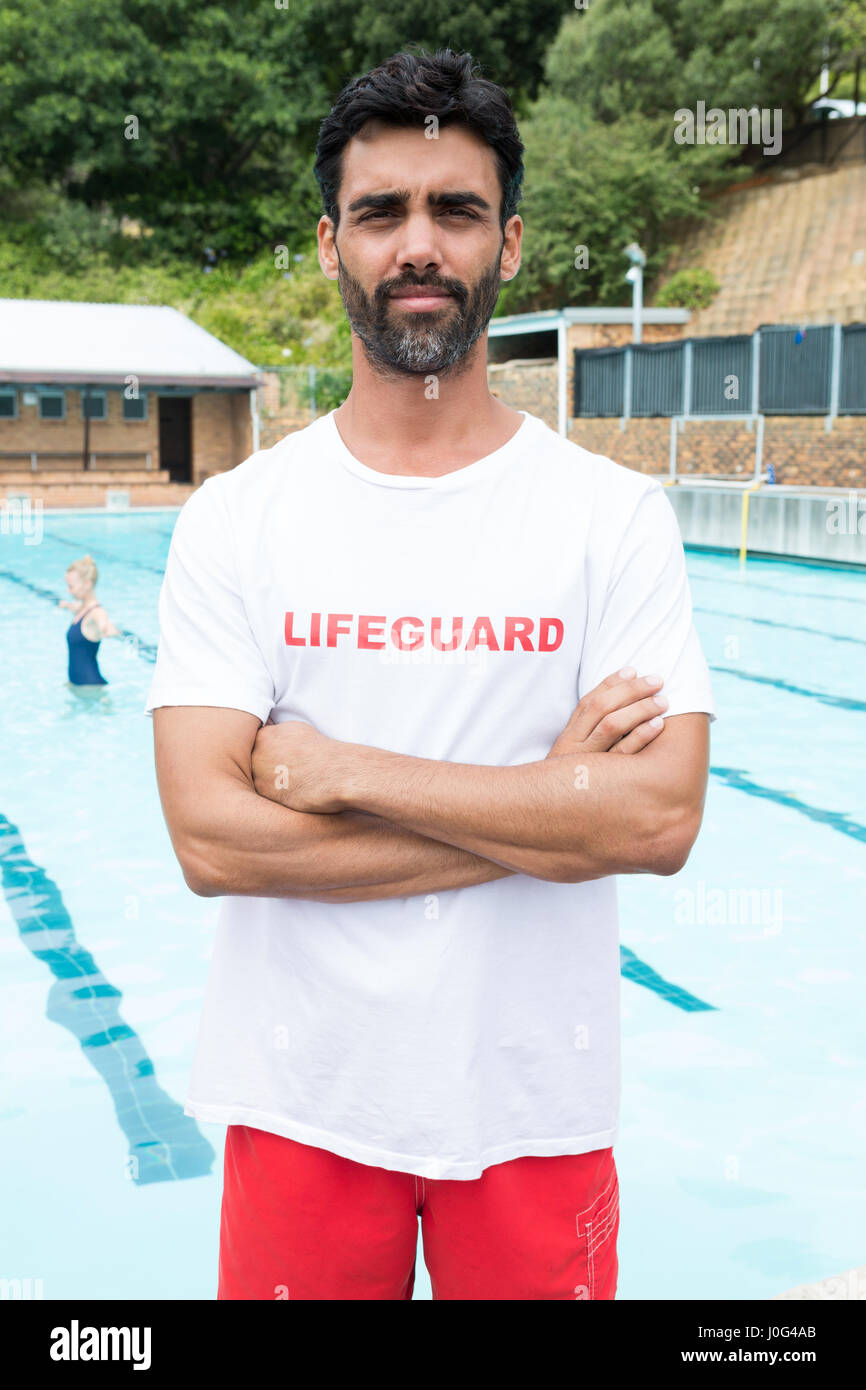Portrait of confident lifeguard standing with arms crossed in poolside ...