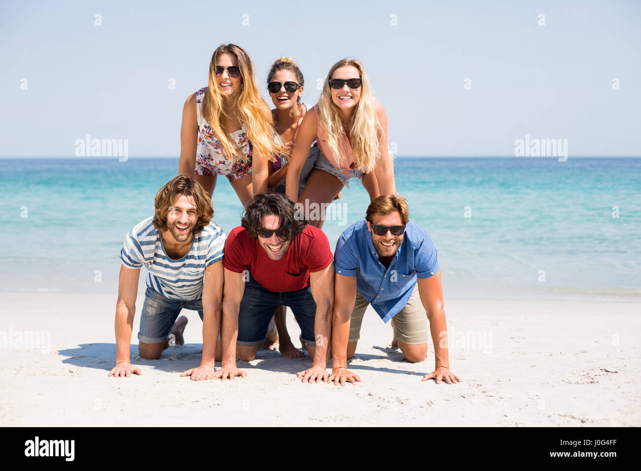 Cheerful friends forming pyramid on shore at beach during sunny day ...